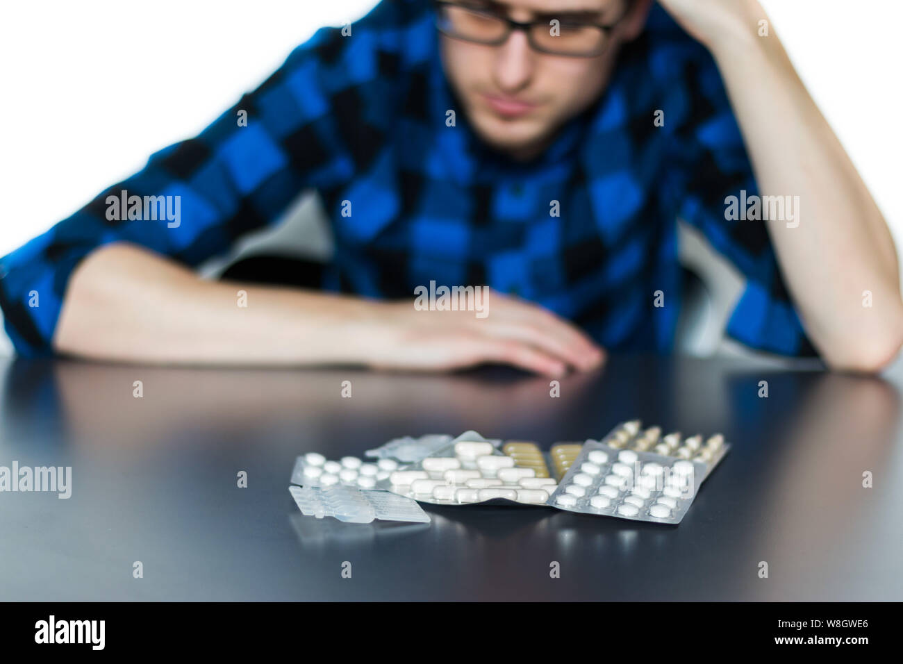 Drug abuse: Young man sitting on a table, drugs and pills in front of ...
