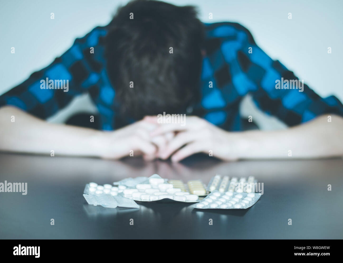 Drug abuse: Young man sitting on a table, drugs and pills in front of ...