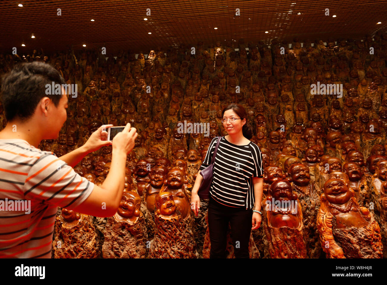 A visitor poses for photos with wooden Buddha statues on display at an ...