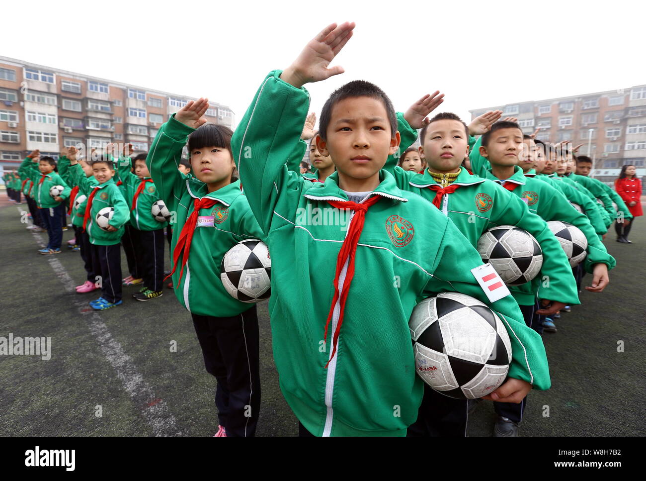 Young Chinese students holding footballs salute during the flag-raising ...
