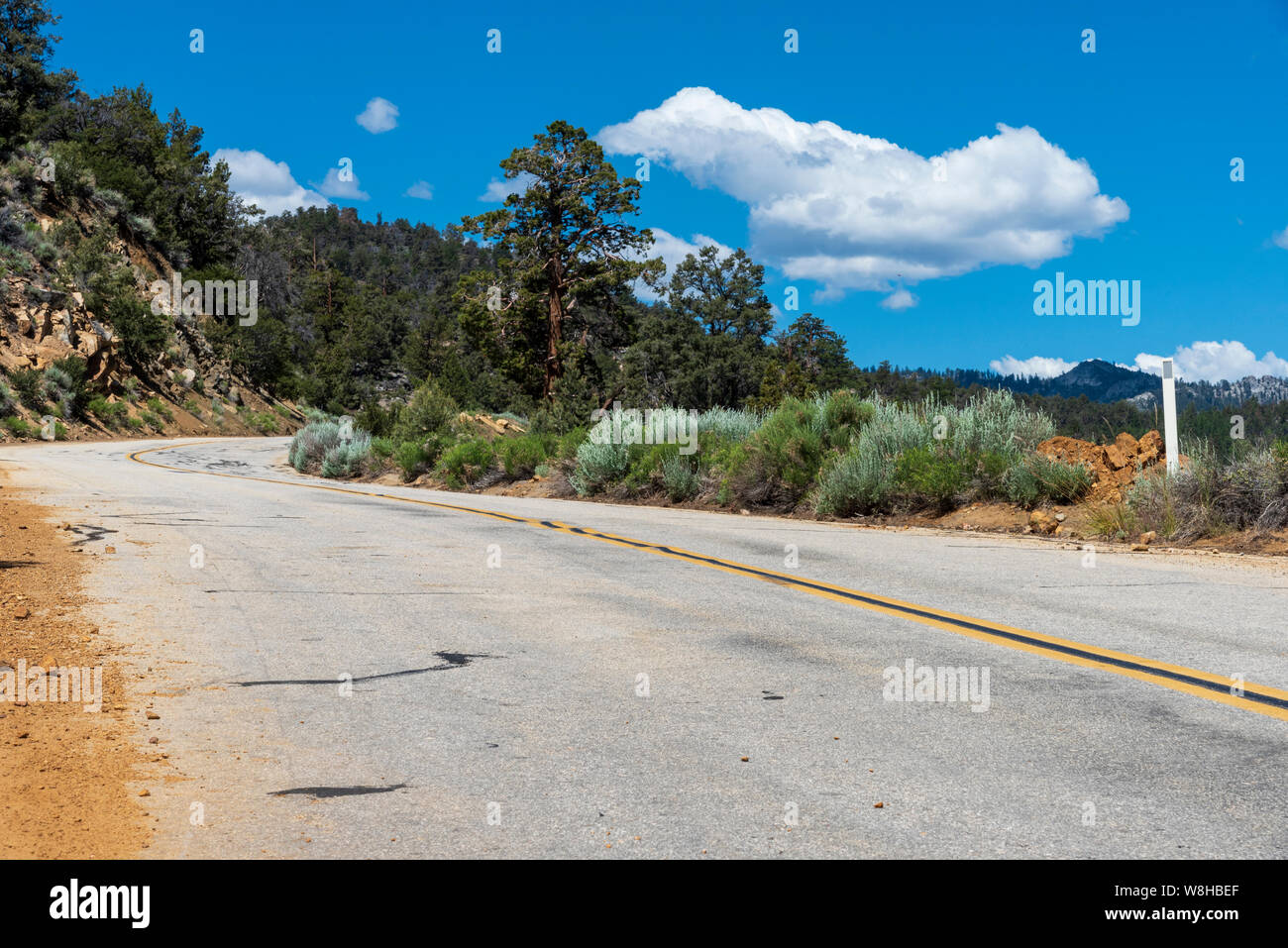 Uphill narrow mountain road with double yellow lines under bright blue ...