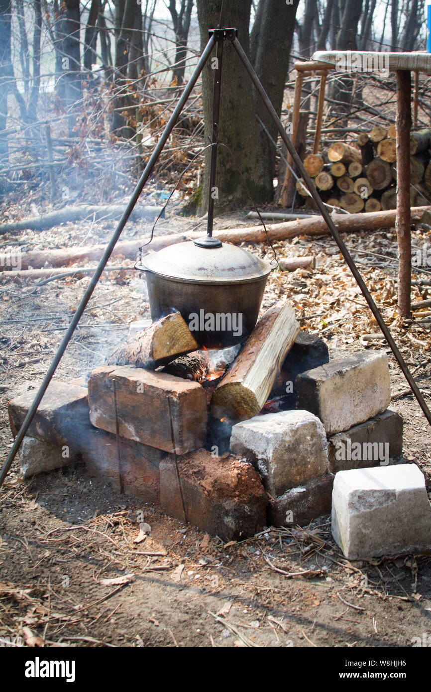 The concept of camping kitchen, on tripod over a fire there is a pot in ...