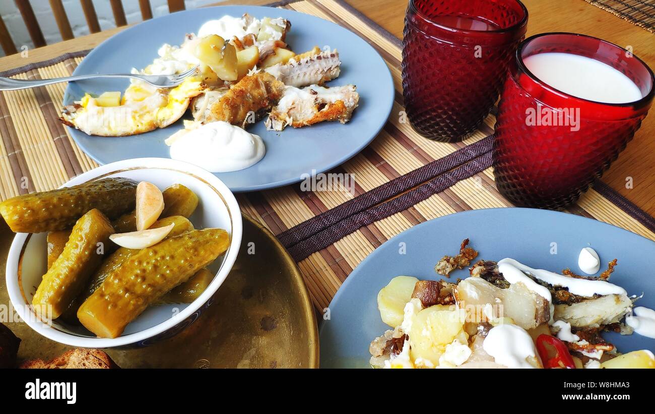 A side view breakfast for two, baked fish and potatoes with pickles ...