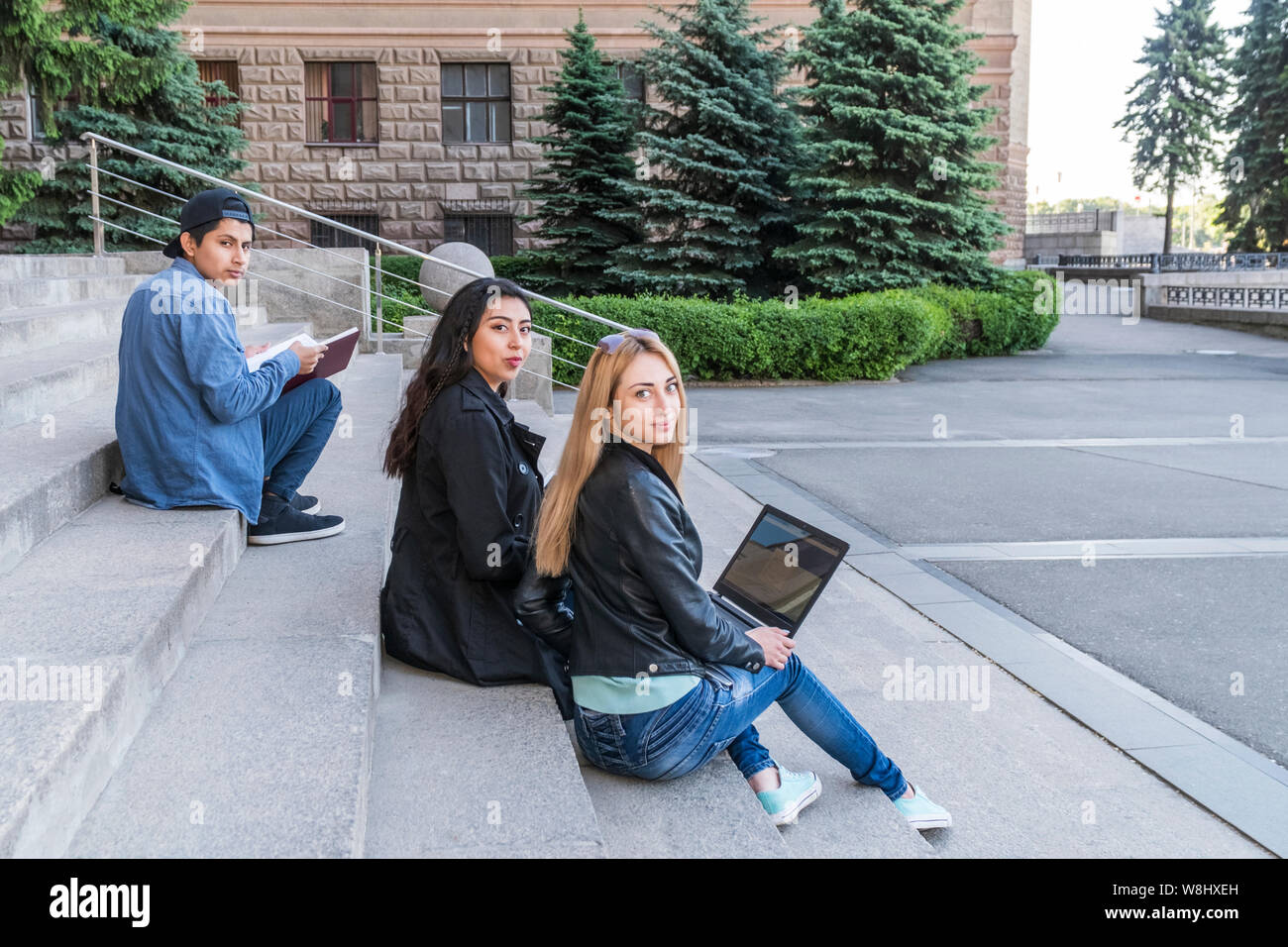 portrait of three students sitting on the stairs of the university ...
