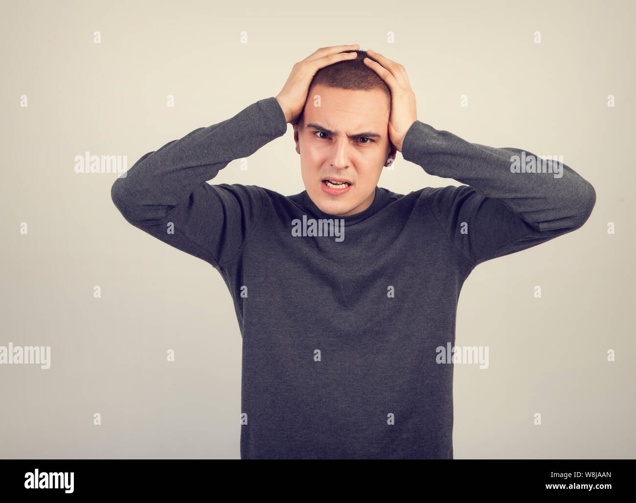 Young casual angry man holding the head two hands on blue studio ...