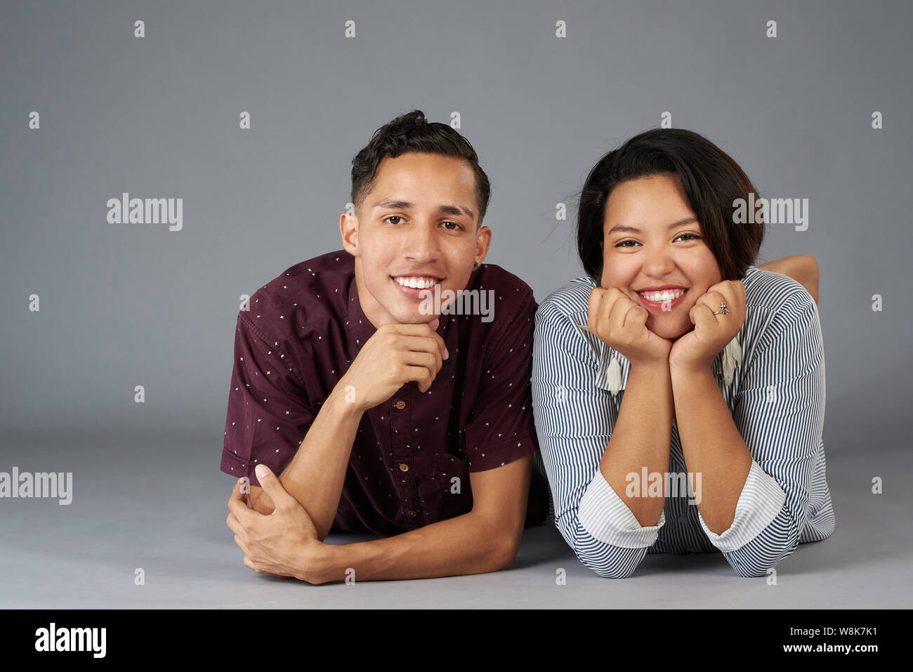 Smiling latin young couple lying isolated on gray studio background ...