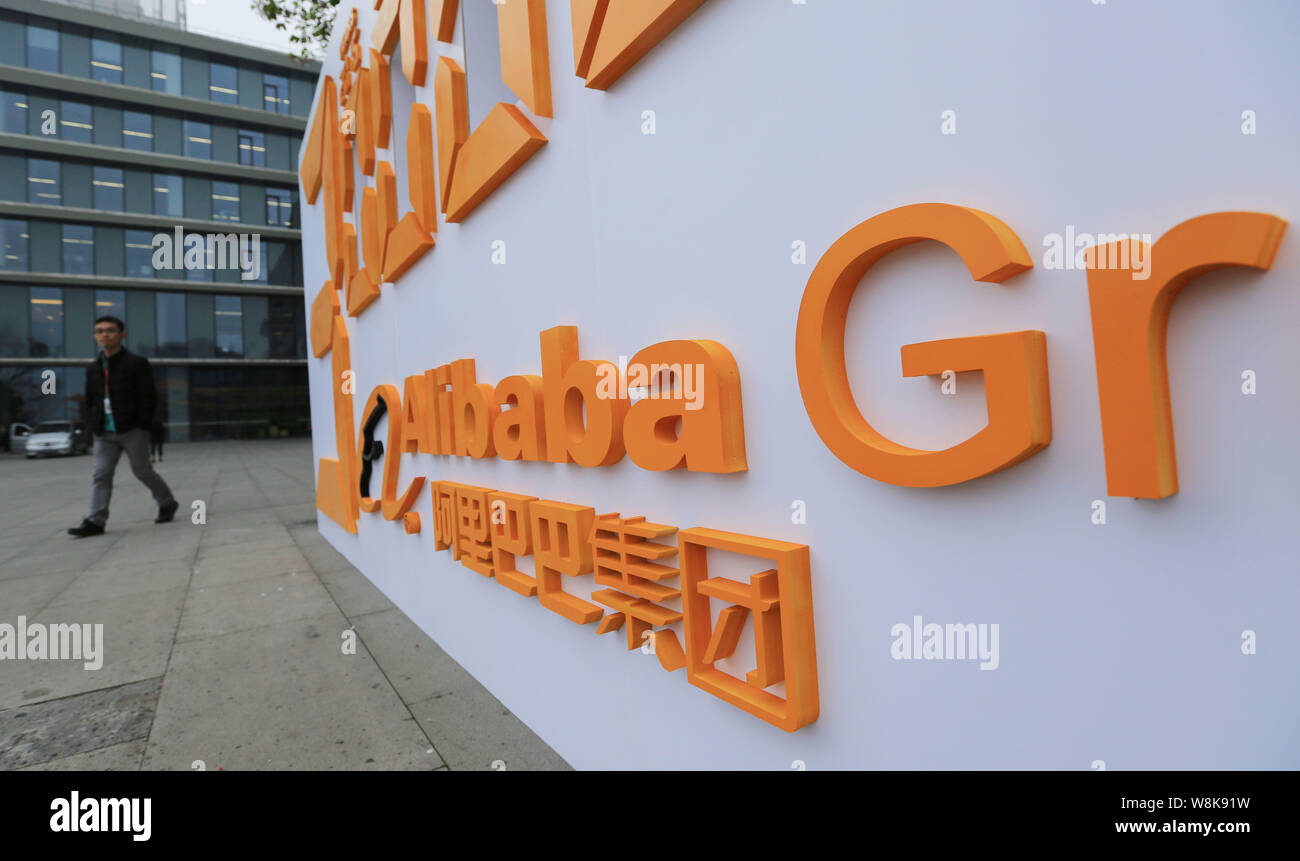 --FILE--A Chinese employee walks past a logo of Alibaba at the ...
