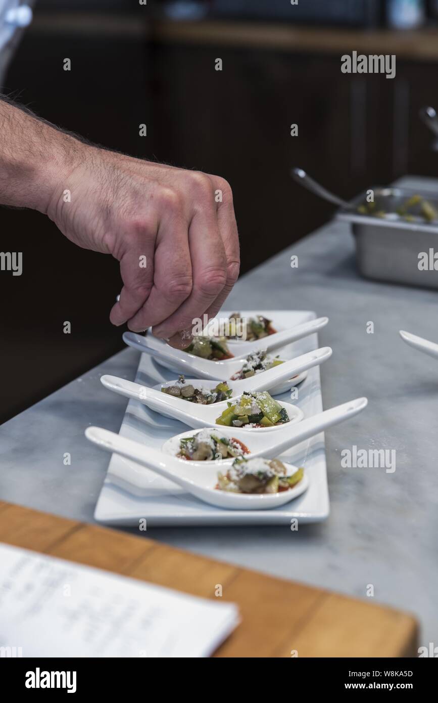 Closeup of a chef's hand fixing appetizers in white spoons on a white ...