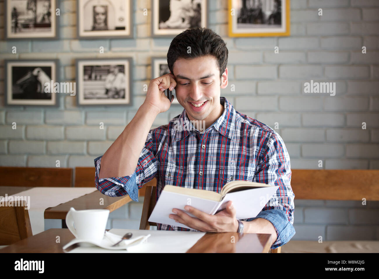 Young man talking on a mobile phone and reading a book in a restaurant ...