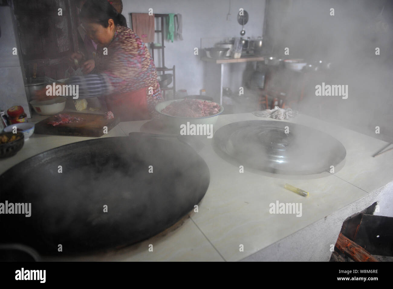 A Chinese villager cooks meat from a butchered pig in the kitchen at ...