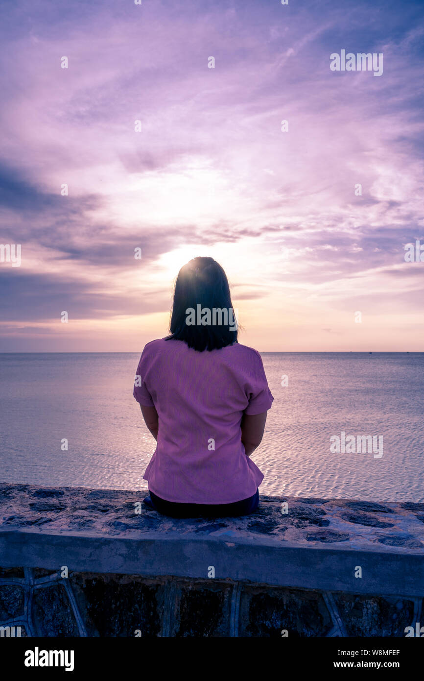 Back view of a woman sitting watching beautiful sunset over the ocean ...