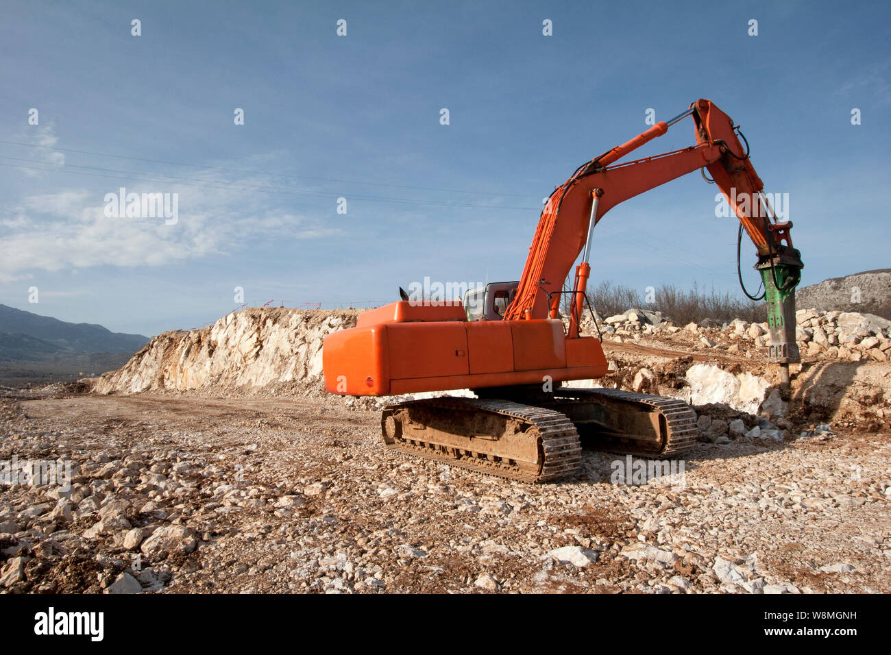 Orange backhoe drilling stone soil on construction of road Stock Photo ...
