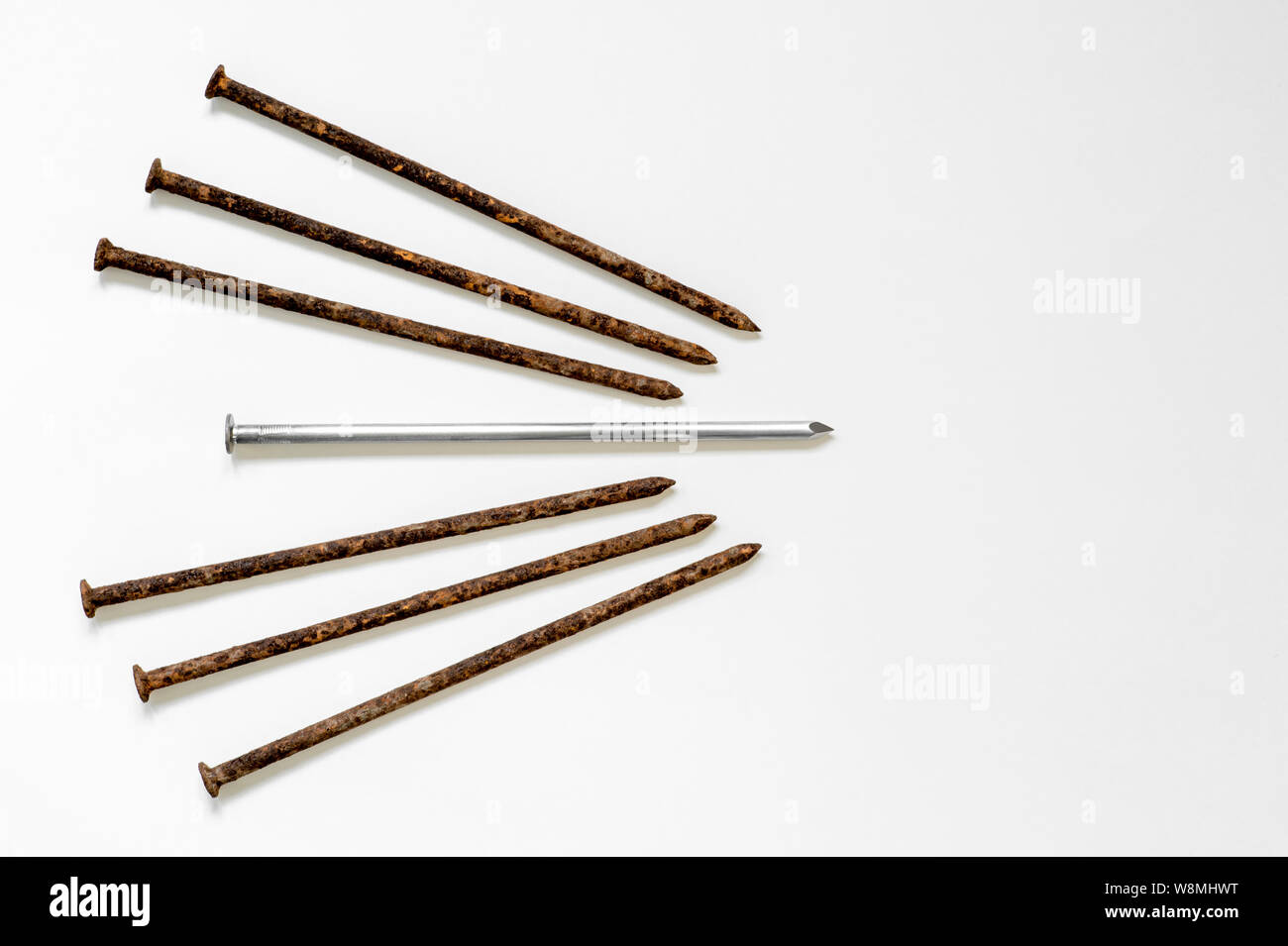 Metal shiny sharp nail in the center of a pile of old rusty nails on a ...
