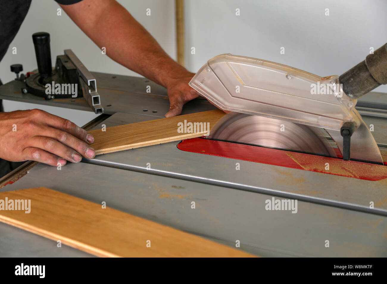 The worker cuts the parquet manually on a circular saw, and the sawdust ...