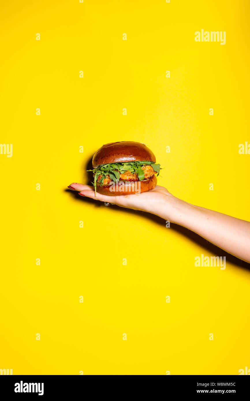 Hand holding burger against yellow background Stock Photo - Alamy
