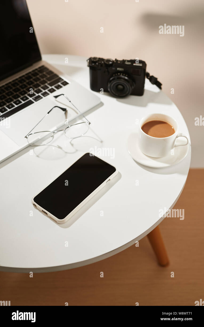 Office desk with mobile phone, coffee cup, laptop, camera and glasses ...