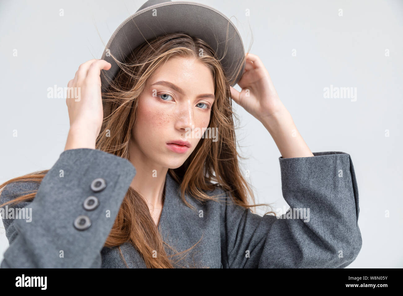 Portrait of cute young woman in grey adjusting hat hair fluttering ...