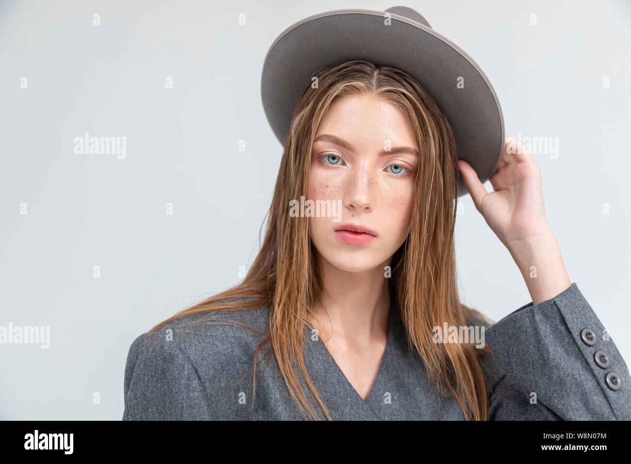 Portrait of trendy brown-haired young woman in grey adjusting hat ...