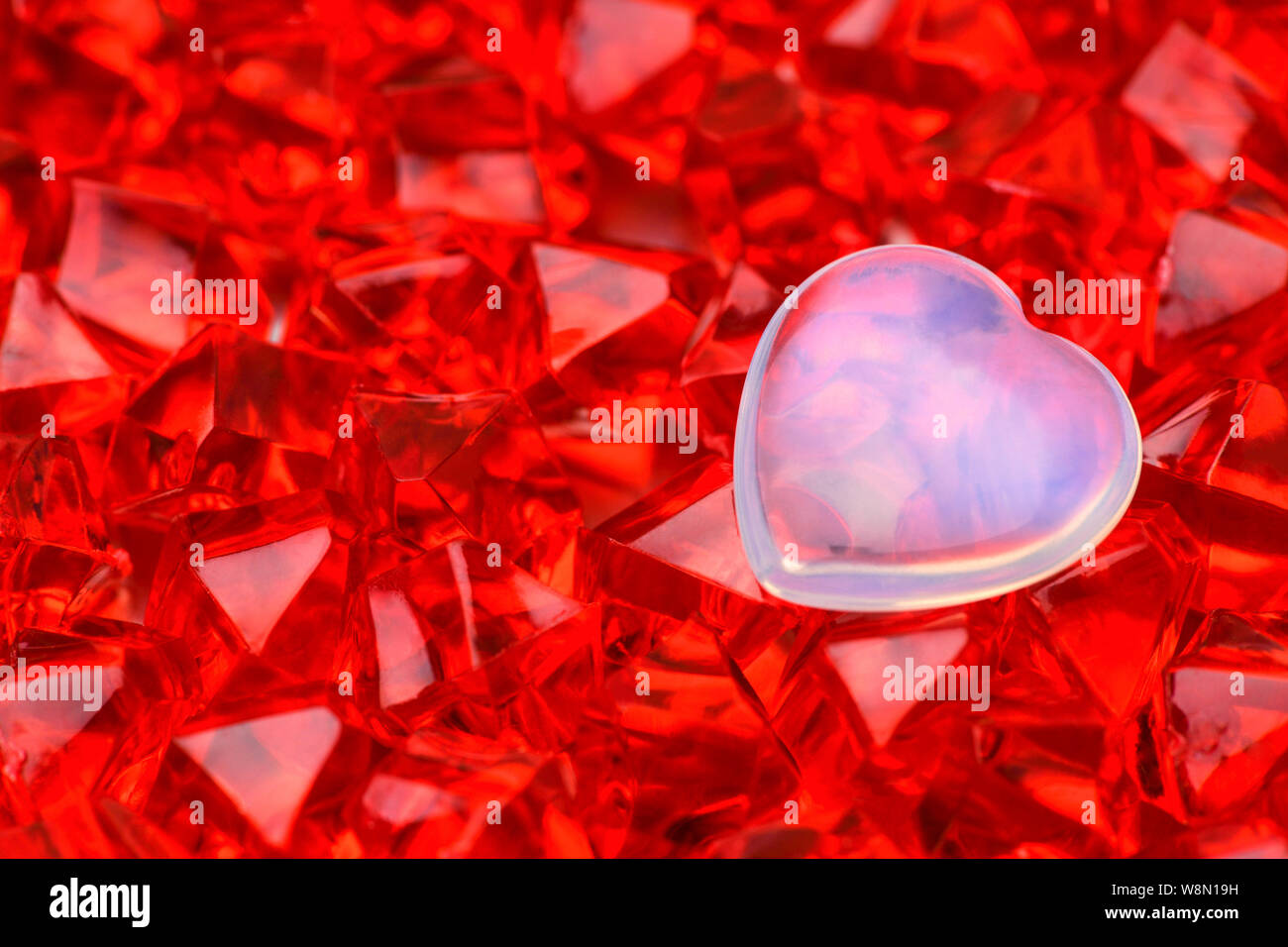 Valentine's day. The white glass heart lies on the red ruby crystals on ...