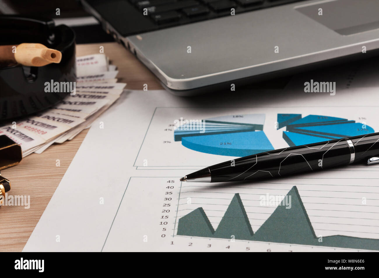 Pen and financial charts on the background of a laptop and cigar ...