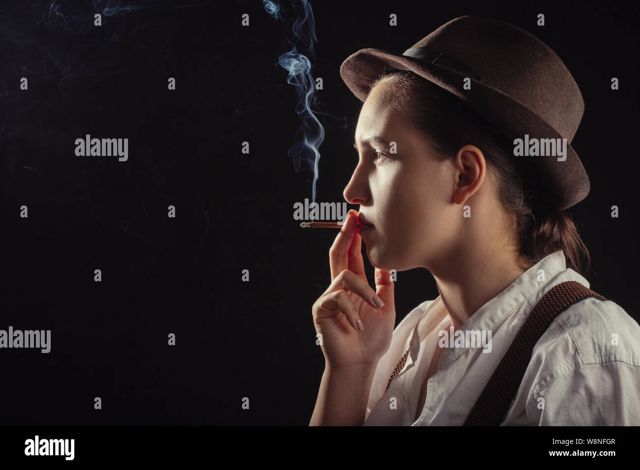 sad serious woman in hat smoking cigarette on black background, profile ...