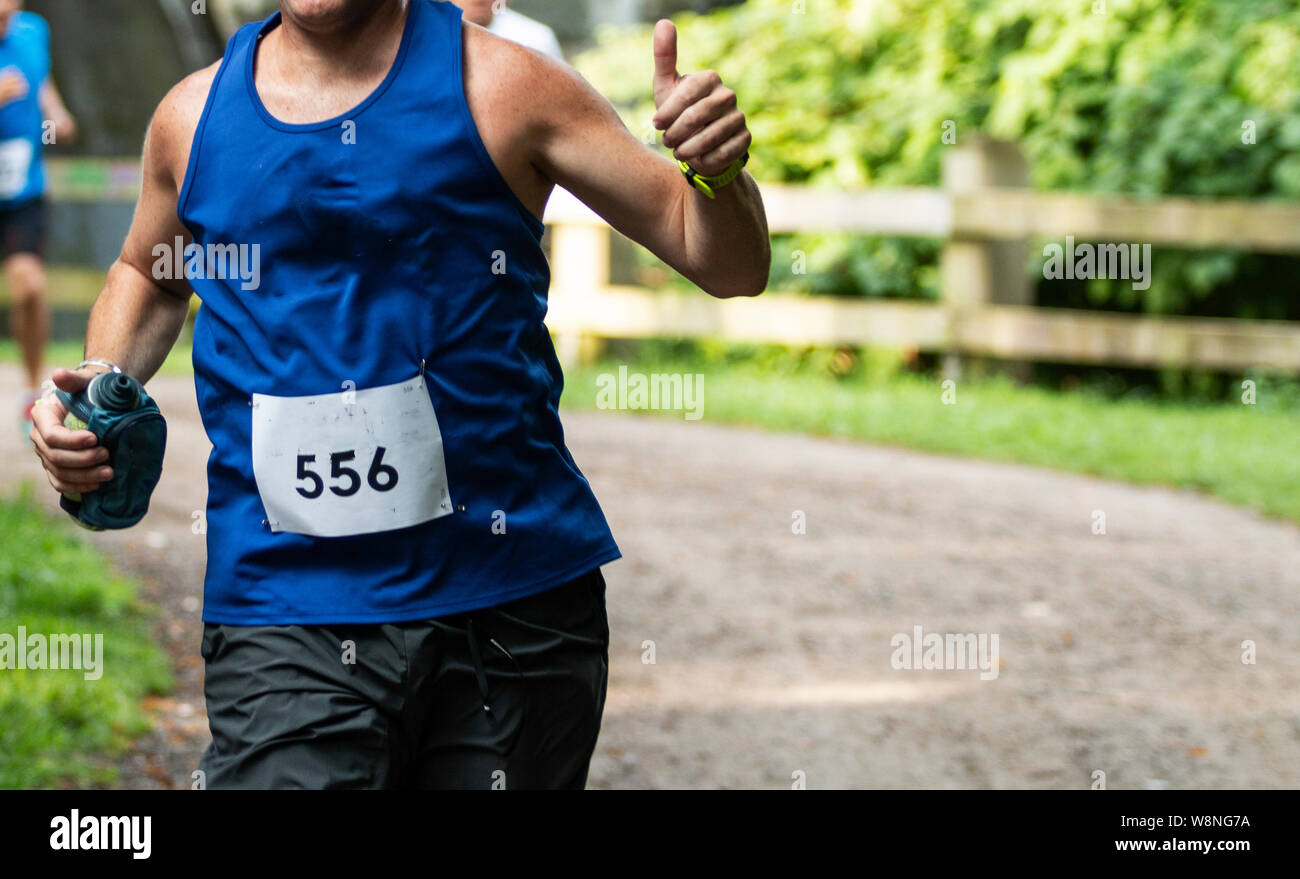 A long distance runner gives a thumbs up during a race on a trail in ...