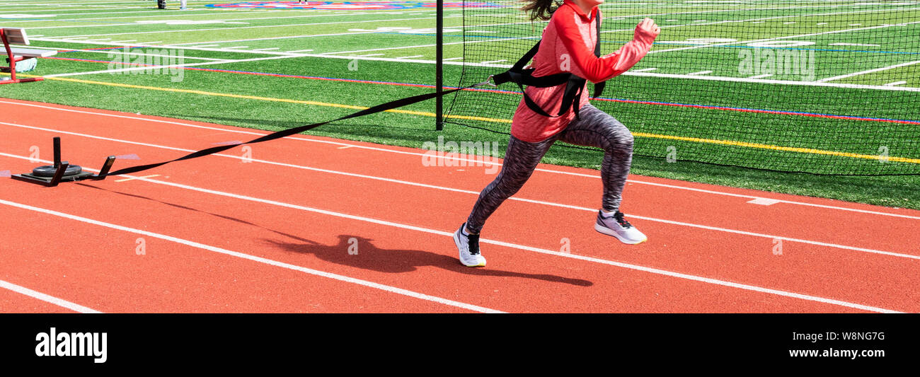 A high school female is pulling a weighted sled while sprinting down a ...