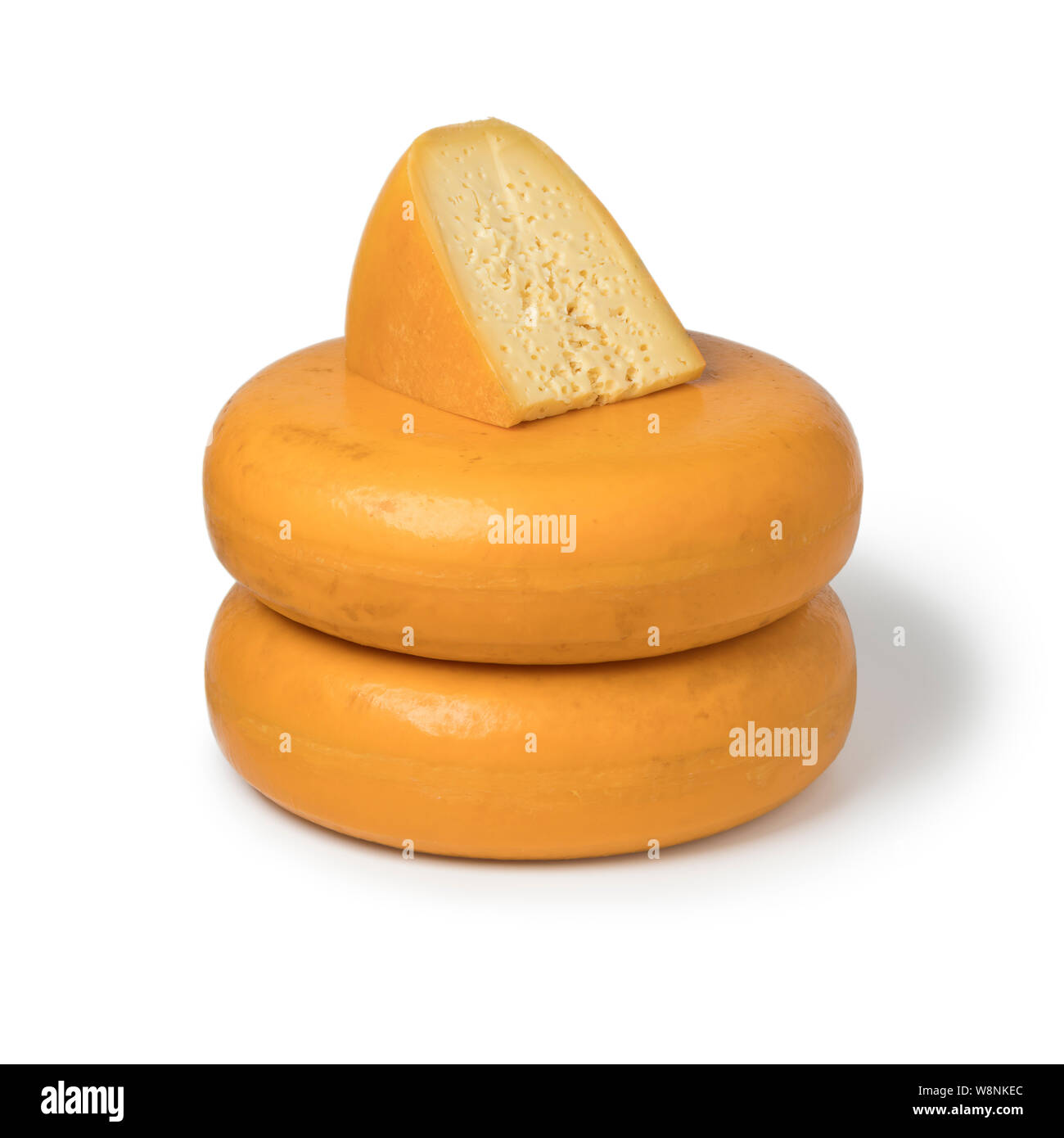 Piece of Dutch Stolwijker cheese on top of two whole round cheeses ...