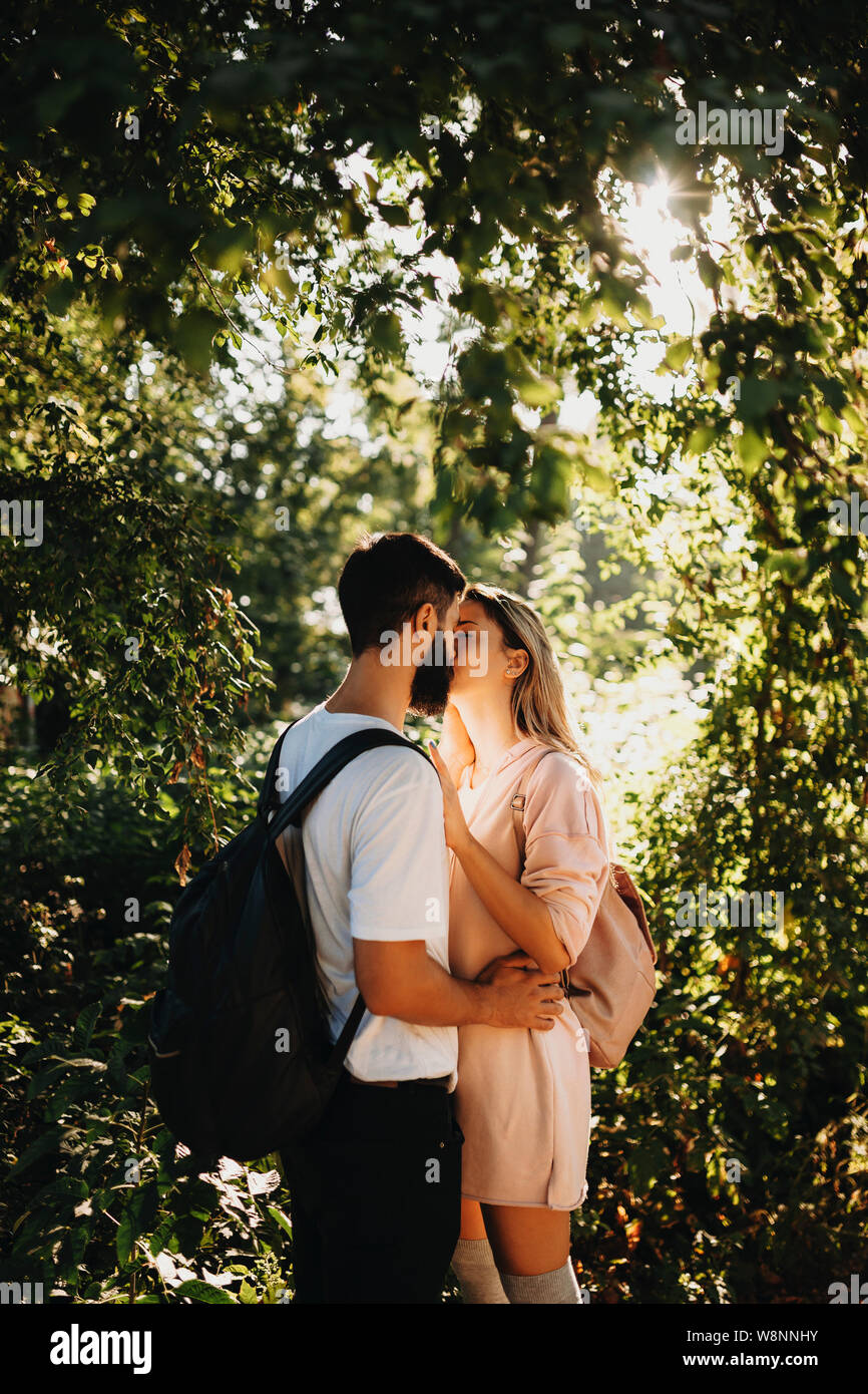 Side view of romantic young couple with backpack standing in green ...