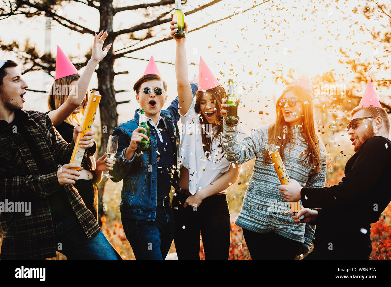 Group of young people raising bottles of beer and exploding party ...