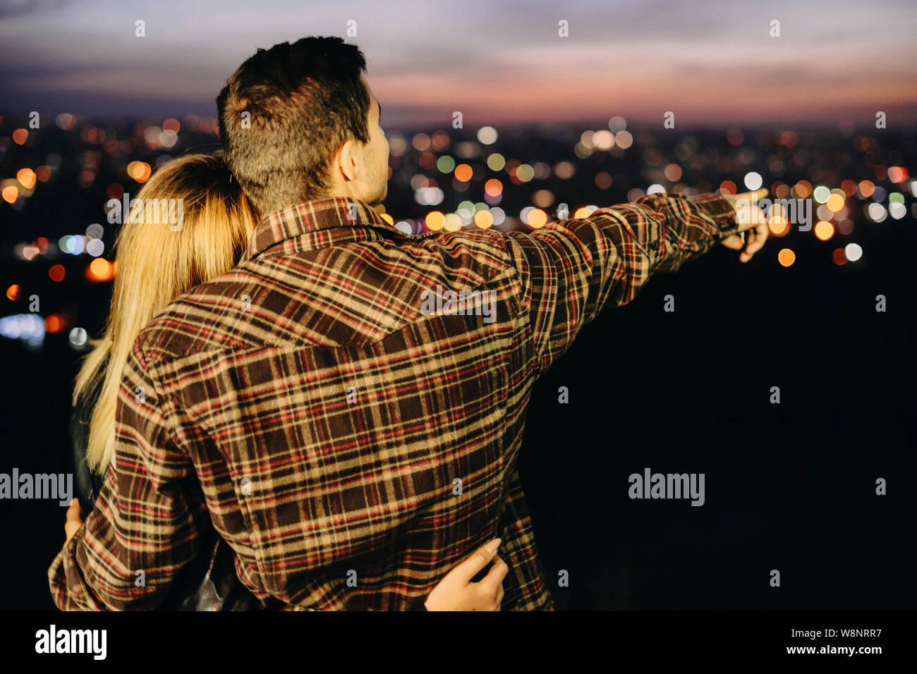 Back view of young guy in checkered shirt hugging girlfriend and ...