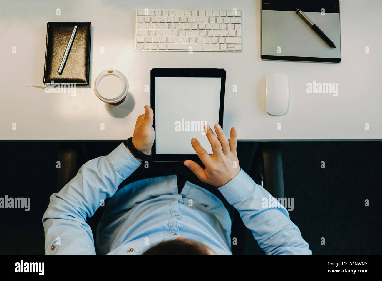 From above crop man sitting at desk in office and tapping on tablet ...