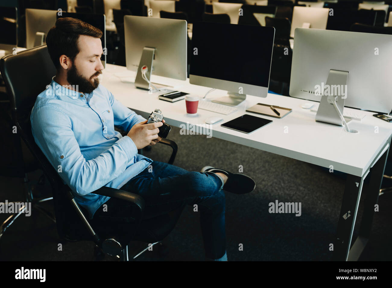 Side view of handsome young man sitting on chair and looking at photos ...