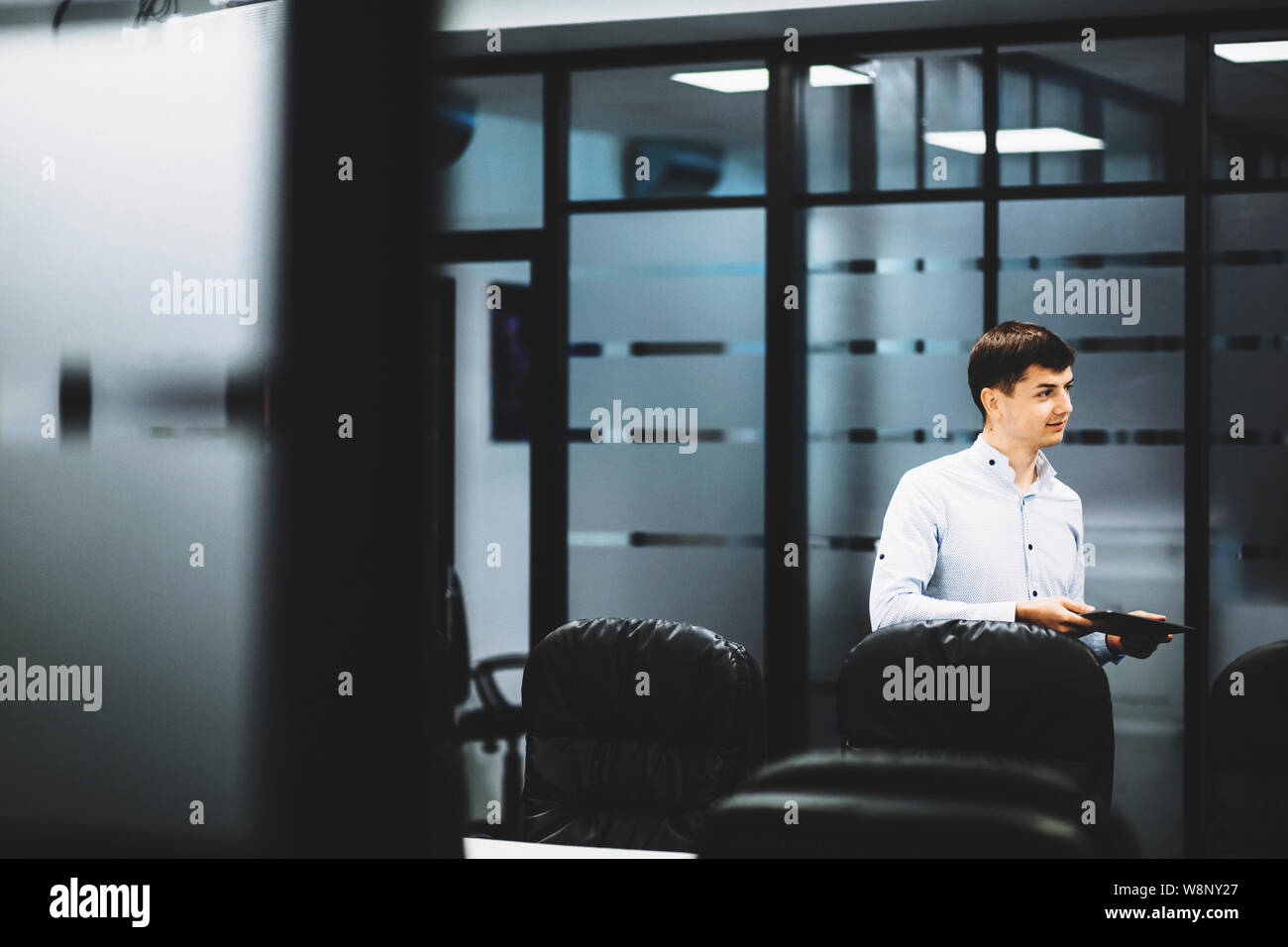 Attractive young man with modern tablet standing near chairs in stylish ...