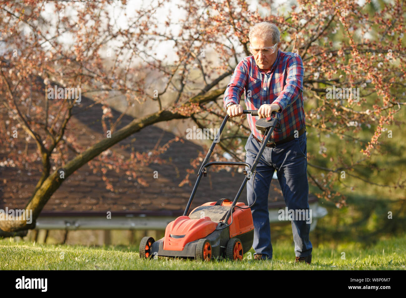 Man with electric lawnmower, lawn mowing. Gardener trimming a garden ...