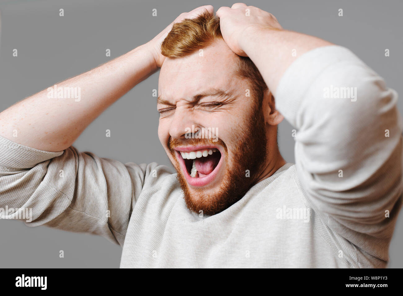 Handsome male tearing ginger hair and screaming in stress while ...
