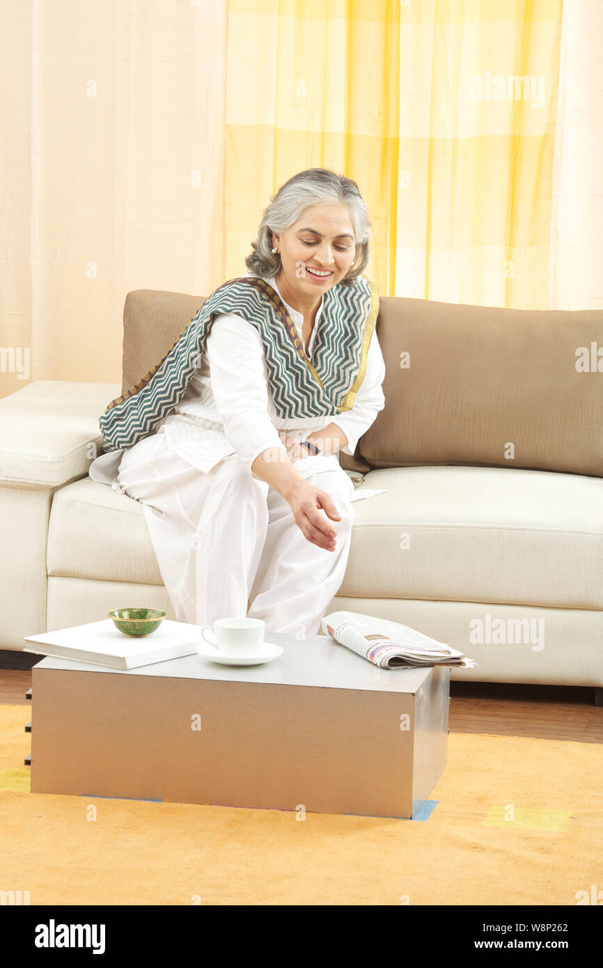 Senior woman picking up newspaper from a table Stock Photo - Alamy