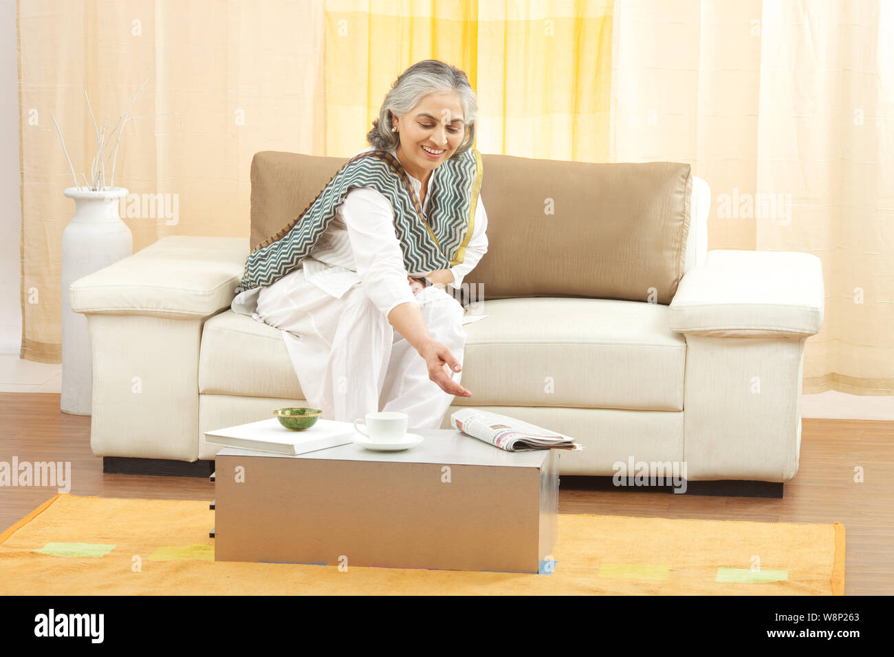Senior woman picking up newspaper from a table Stock Photo - Alamy