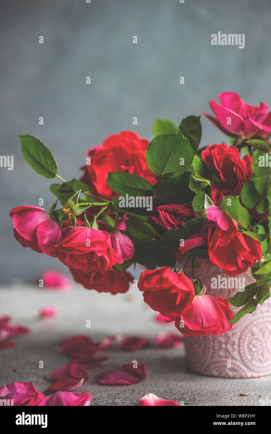 Red tea roses bouquet in ceramic vase on the concrete table as a ...
