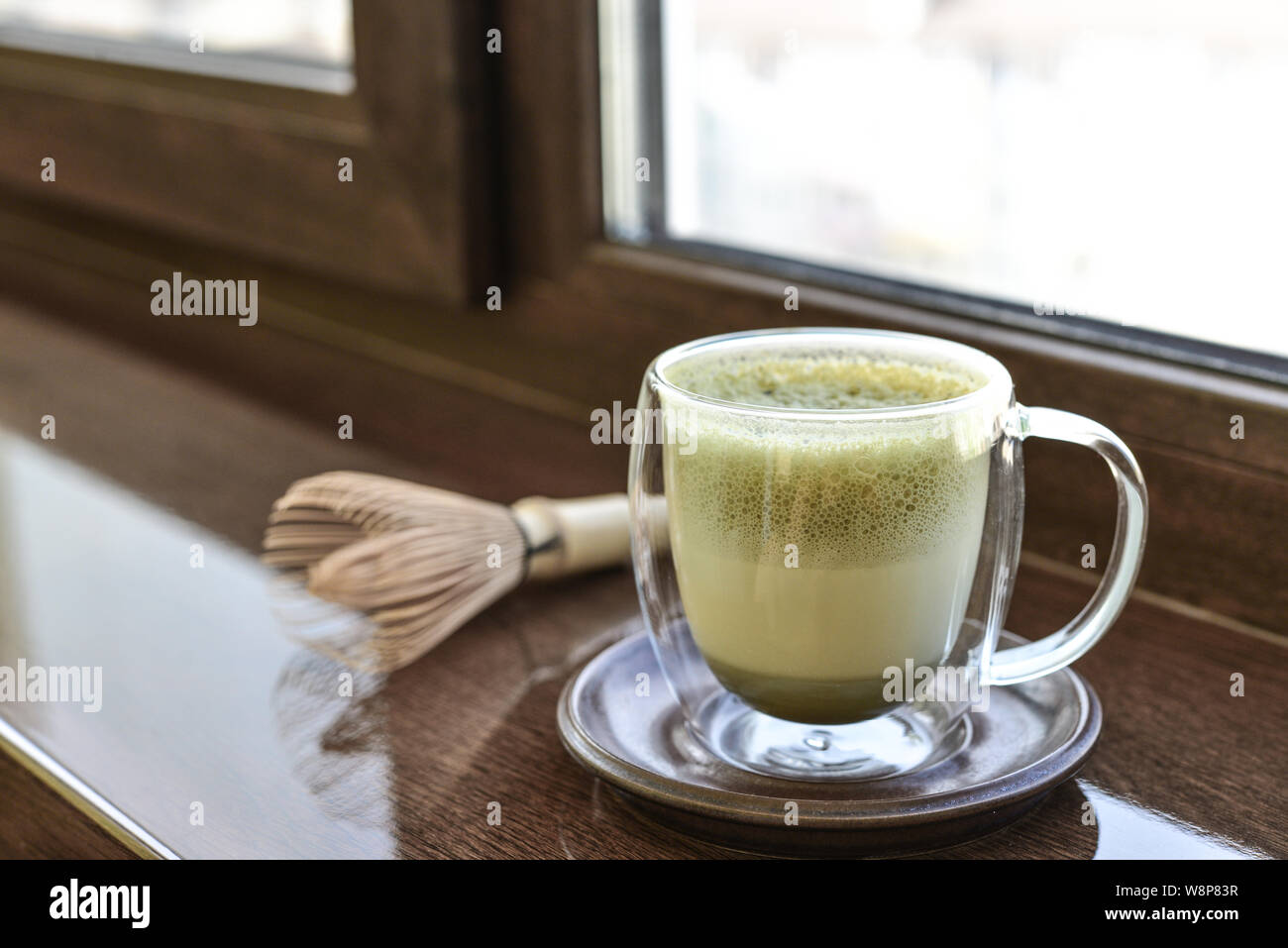 Matcha green tea latte with matcha powder and bamboo whisk on window ...