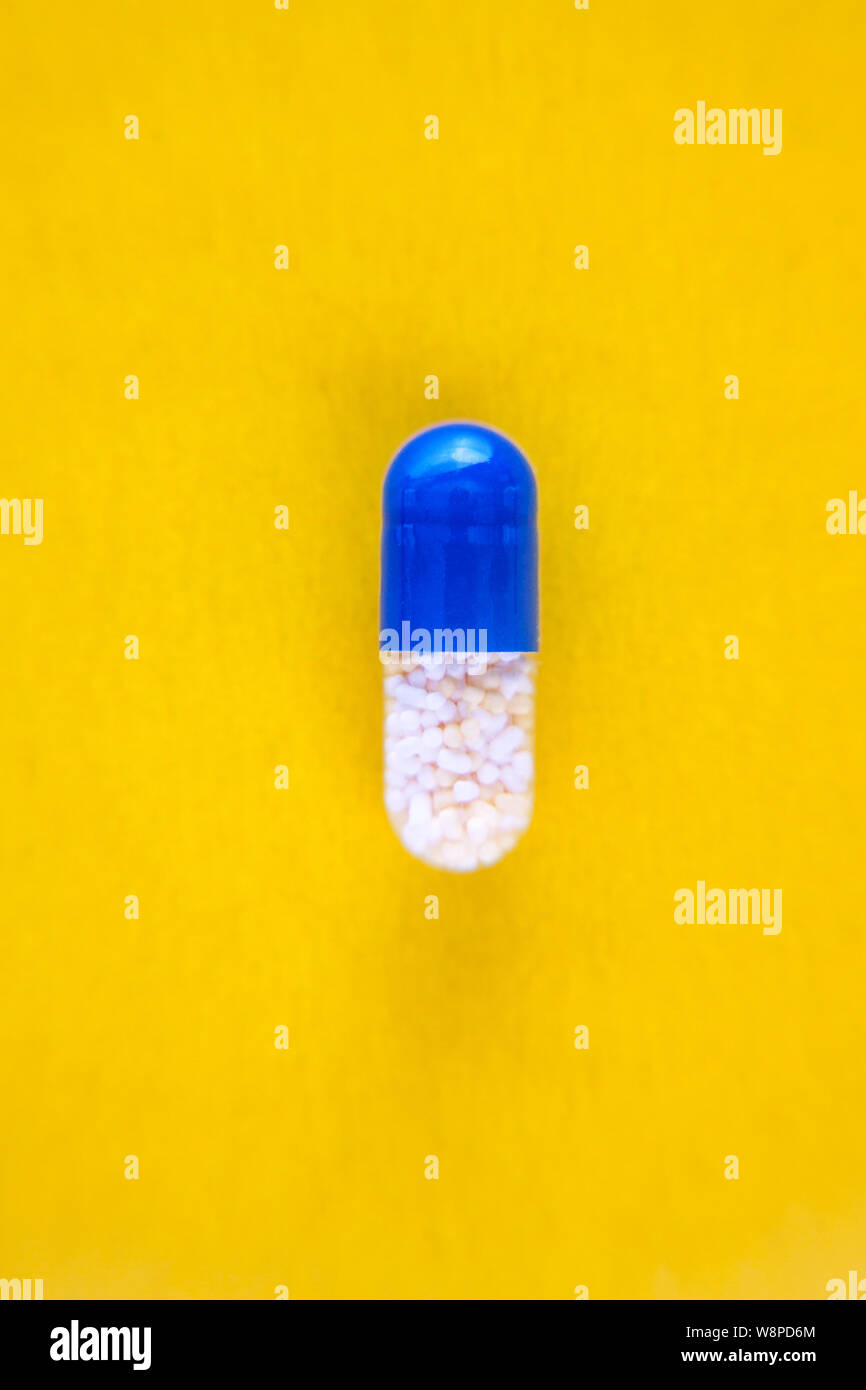 one blue pill capsule isolated on yellow background, close-up, top view ...