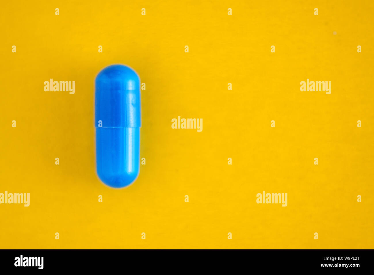 one blue pill capsule isolated on yellow background, close-up, top view ...