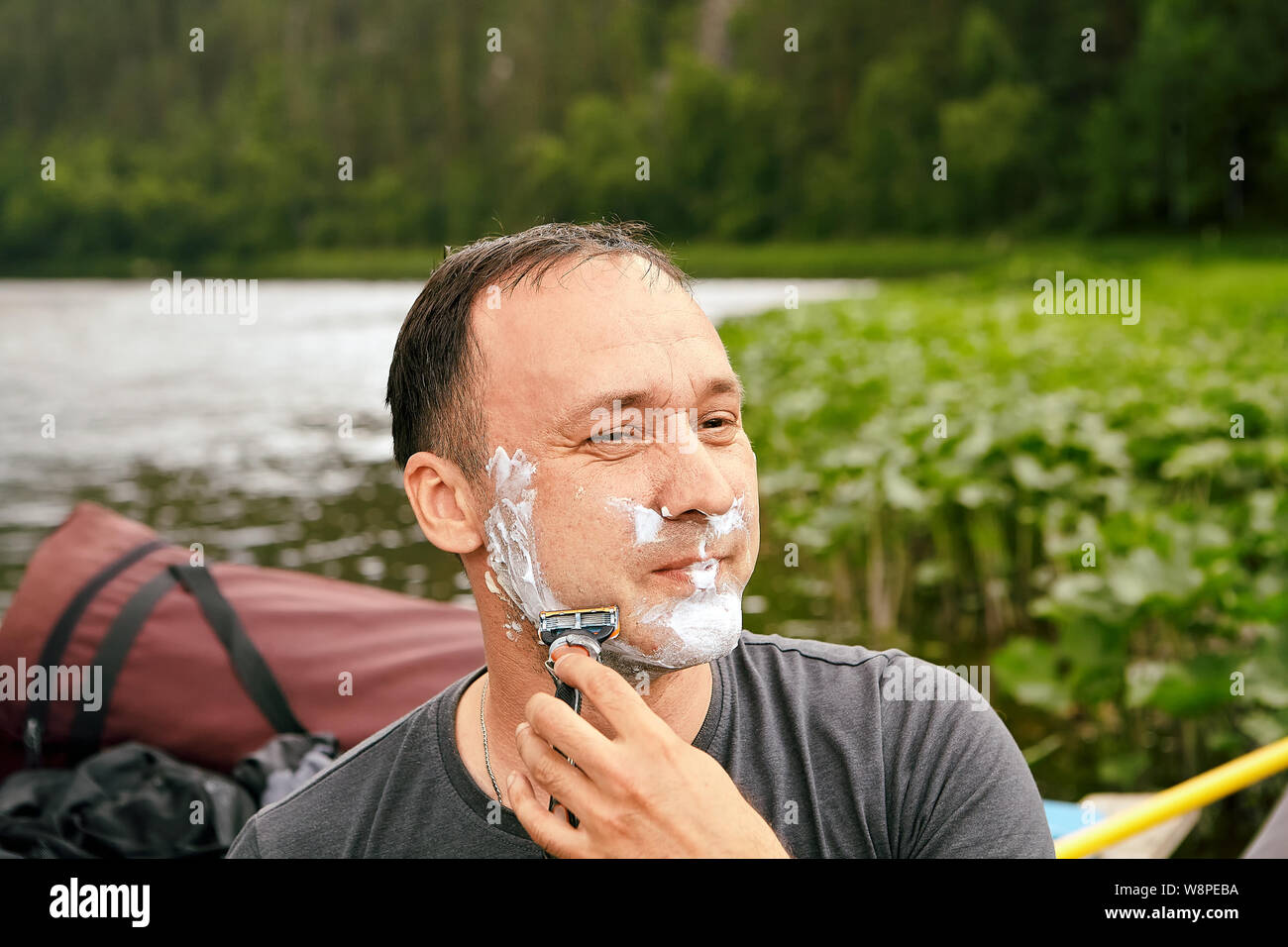 Caucasian man is shaving his face with help of foam and razor blade in ...