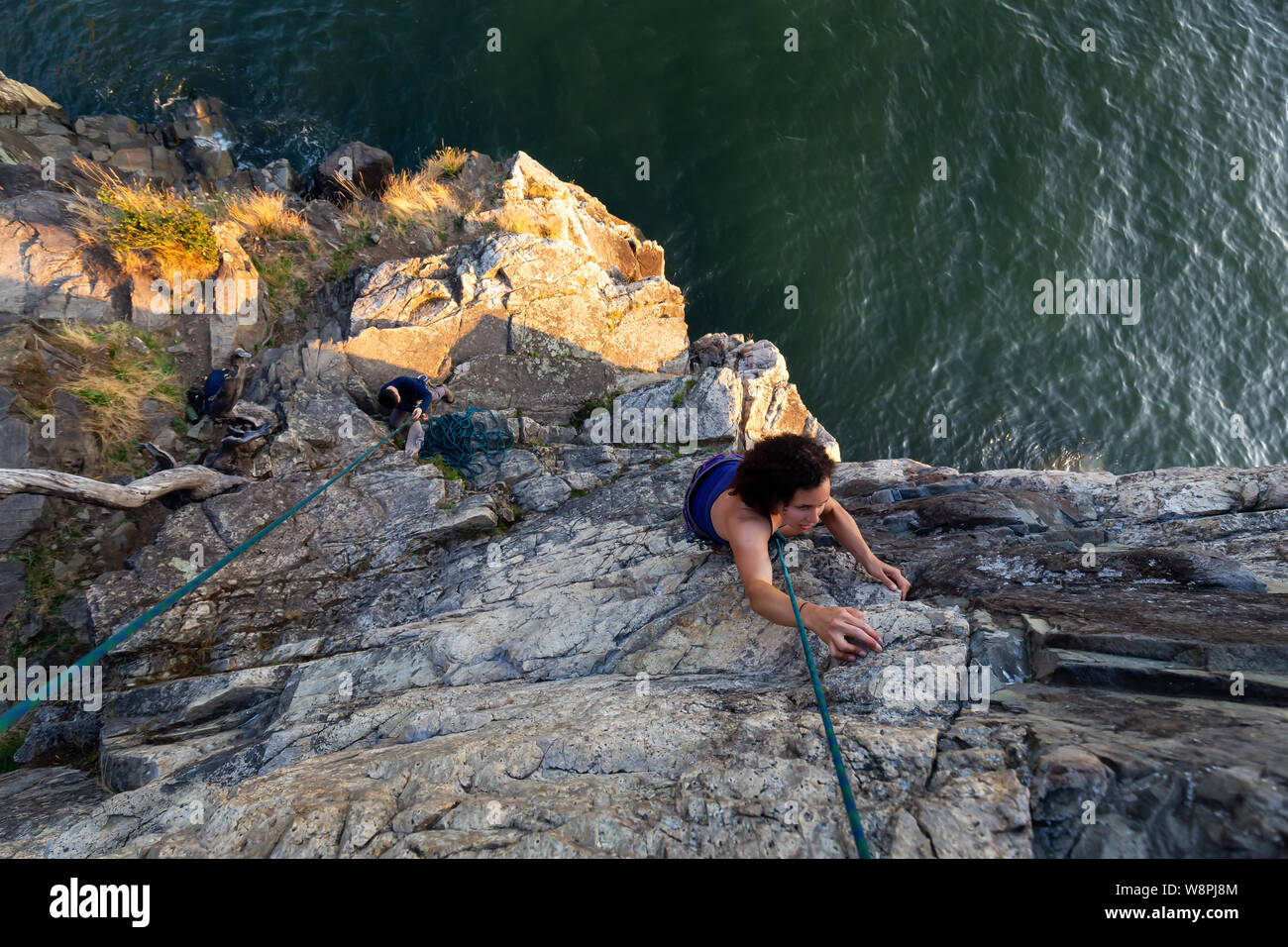 Adventurous Girl is Rock Climbing up a Steep Cliff during a summer ...