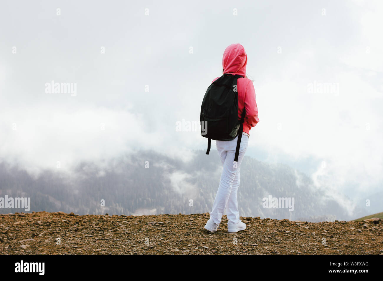Tween girl with backpack looking on beautiful mountains in the clouds ...