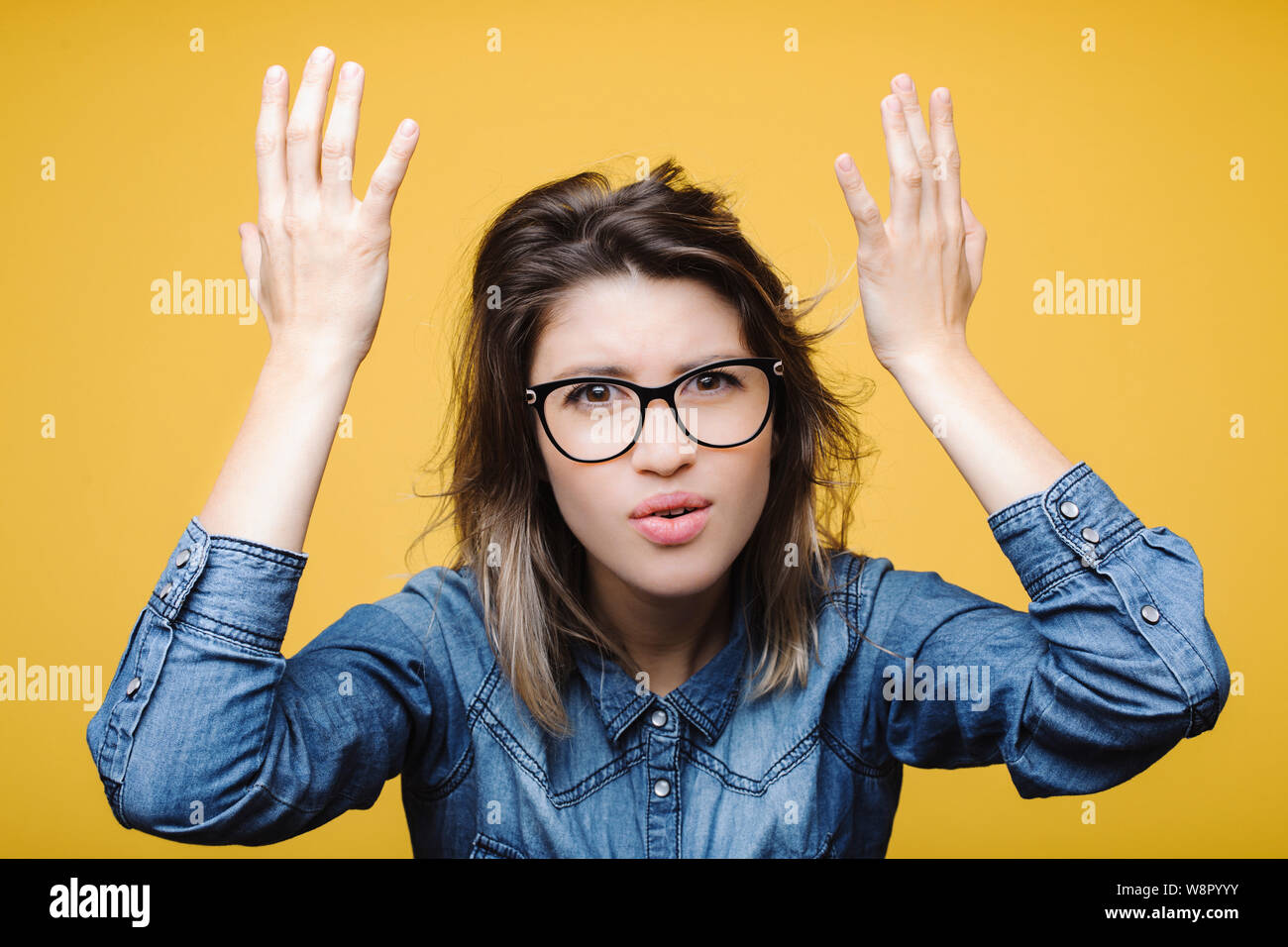Attractive young confused lady in jean shirt with upped hands looking ...