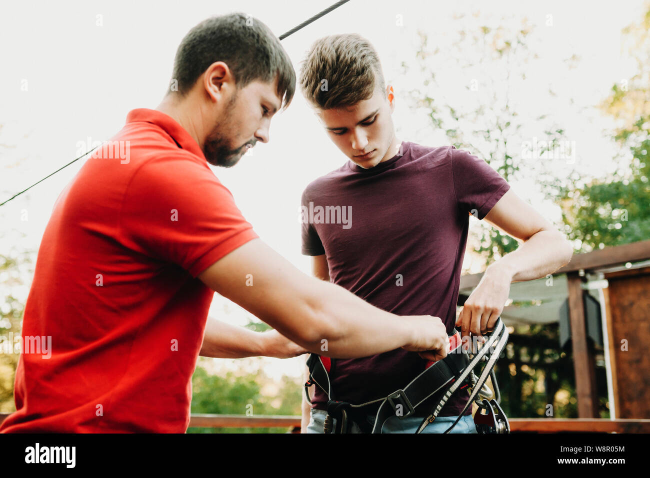 Adult staff man helping young guy with wearing safety harness gear ...