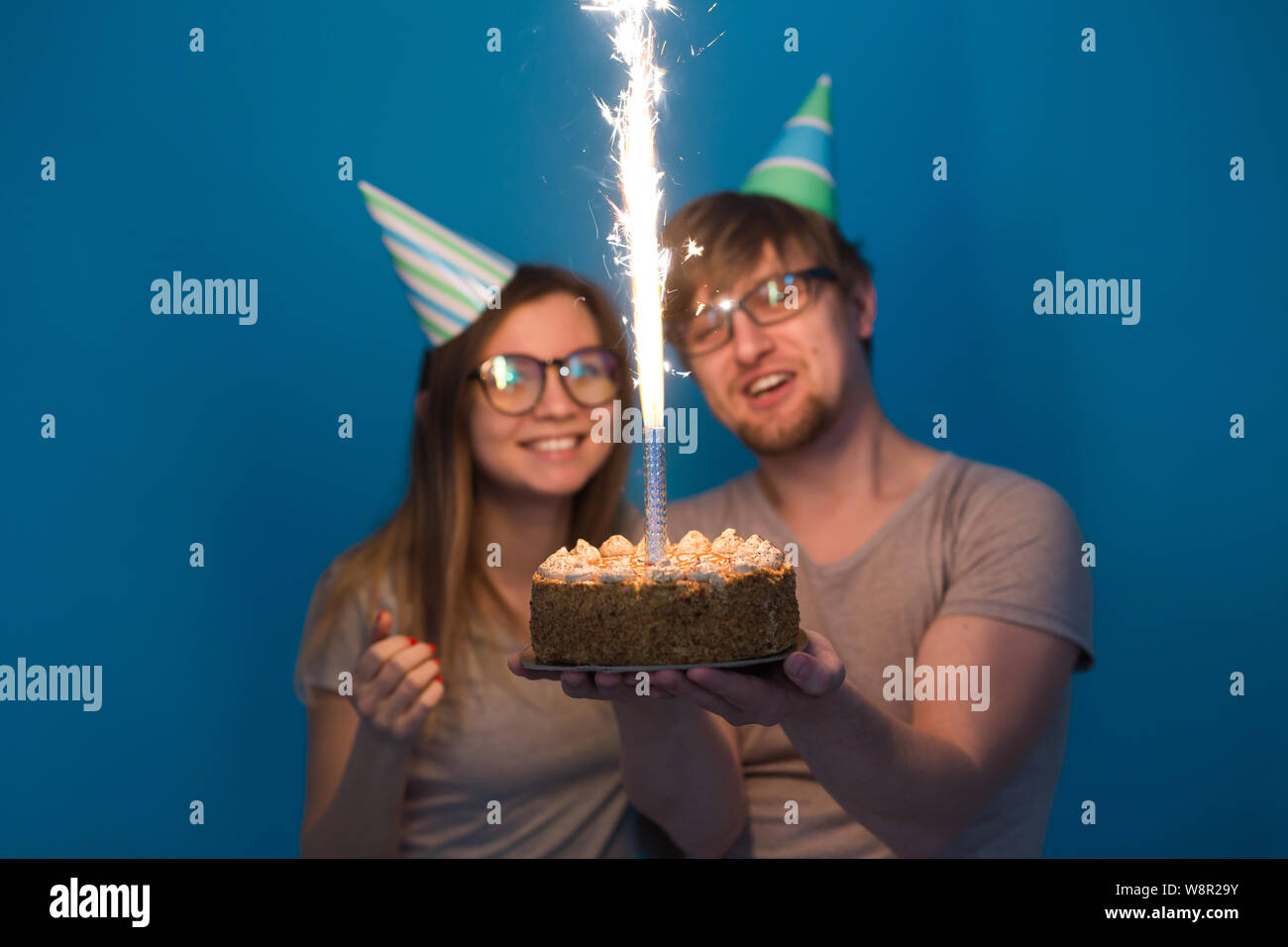 Funny young couple in paper caps and with a cake make a foolish face ...