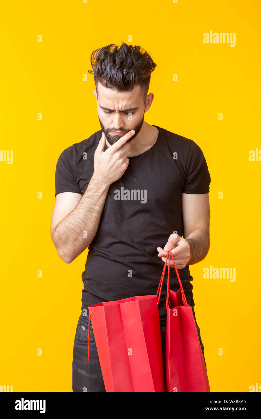 Cute young sad bearded man looks at the purchase in shopping bags on a ...