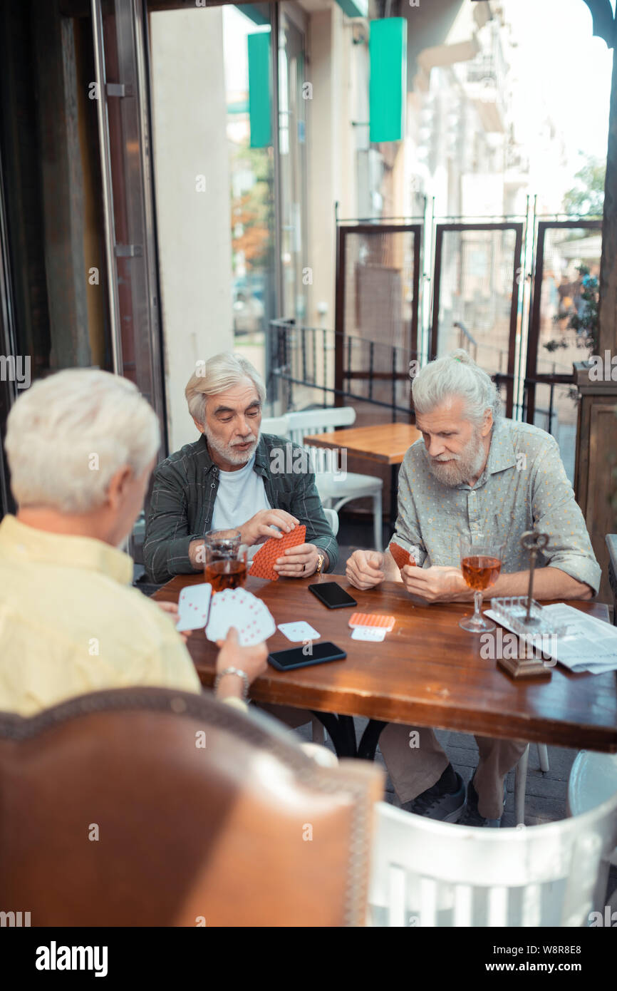 Retired men playing cars while sitting outside pub Stock Photo - Alamy